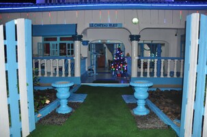 Maquete de uma casa com uma placa indicando "LE CHATEAU BLEU" e um pinheiro de Natal decorado.