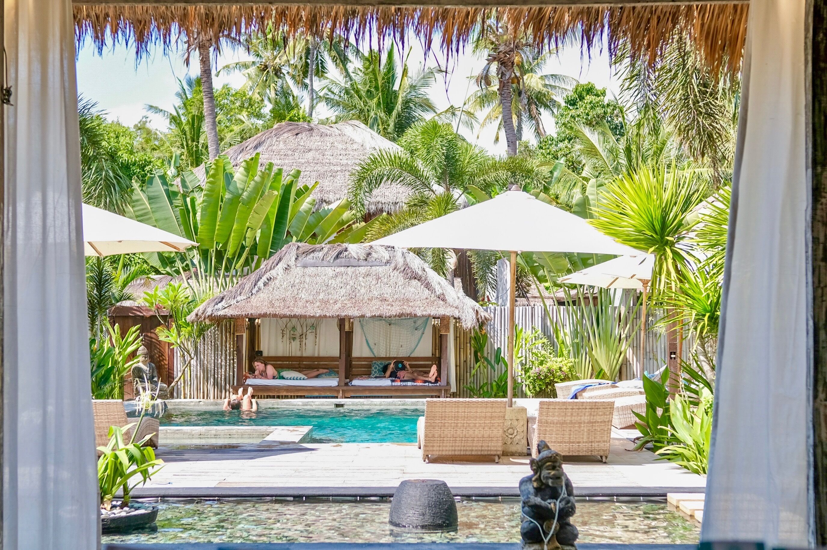 Uma área de piscina com estruturas de telhado de palha, espreguiçadeiras e plantas tropicais.