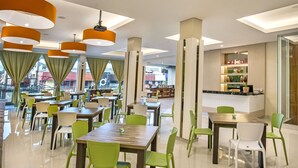 Uma área de jantar moderna com várias mesas e cadeiras, um bar e janelas amplas com cortinas.