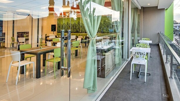 Uma sala de jantar moderna com divisórias de vidro, cortinas verdes e vista para a cidade.