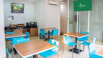 Uma área de refeições de hotel com mesas e cadeiras, um balcão com alimentos e uma placa indicando o nome do hotel.