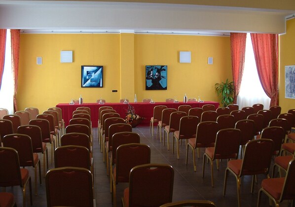 Uma sala de conferências com fileiras de cadeiras, um pódio e duas obras de arte emolduradas nas paredes.