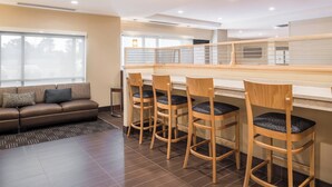 Uma área de bar moderna com banquetas de madeira e um sofá ao fundo.