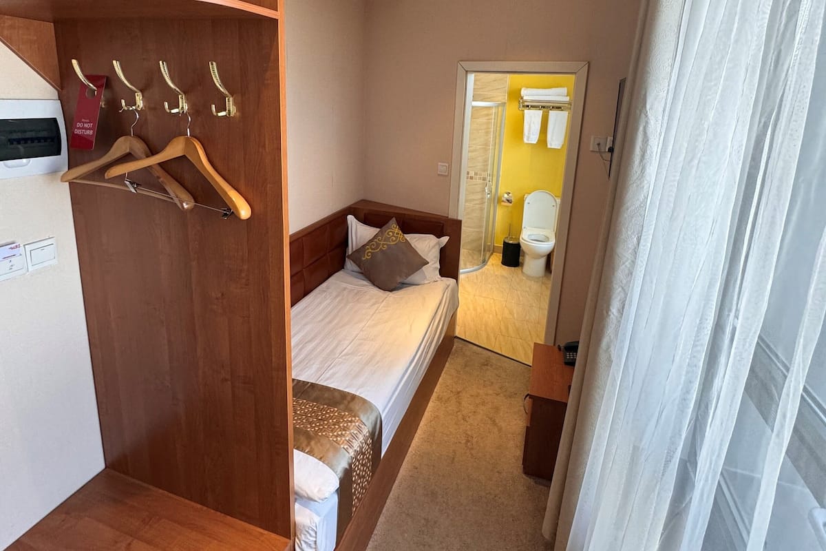 Quarto de hotel com cama, guarda-roupa de madeira, mesa de cabeceira e banheiro visível por uma porta aberta.