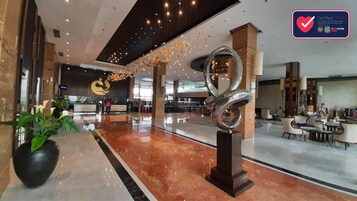 Um hall amplo com piso de mármore polido, uma grande escultura metálica e uma área de recepção com uma tela digital.