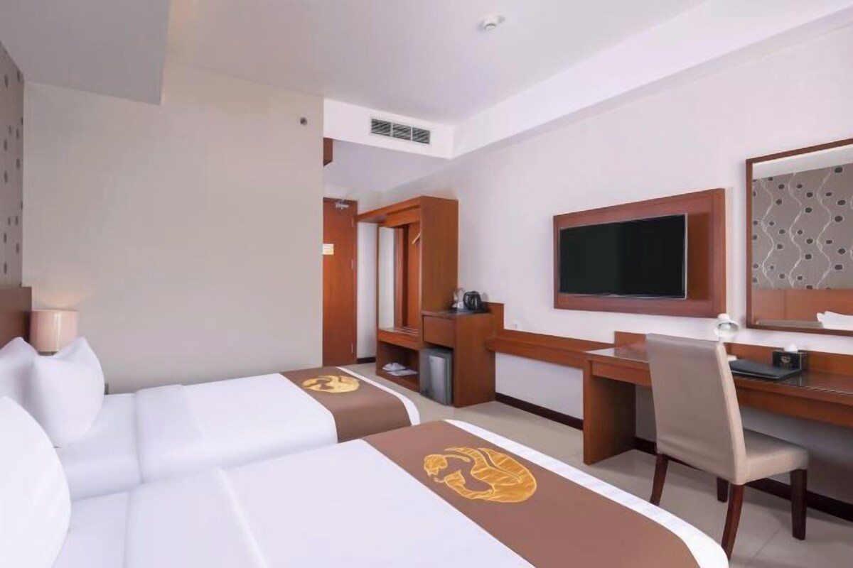 Quarto de hotel com duas camas, uma escrivaninha, uma cadeira, uma televisão e um guarda-roupa.