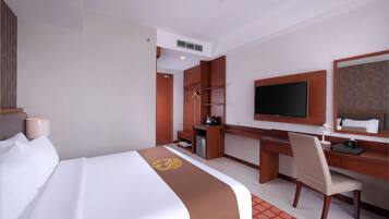 Quarto de hotel com cama, escrivaninha, cadeira, televisão e guarda-roupa.