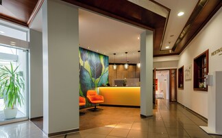 Uma área de recepção com design moderno, destacando um balcão de atendimento, um mural abstrato vibrante e um espaço de estar com cadeiras laranja.