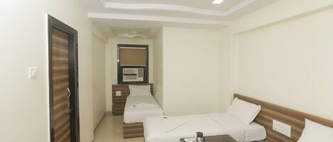 Quarto de hotel com duas camas de solteiro, cabeceira de madeira, uma mesa pequena com um controle remoto e um ventilador de teto.