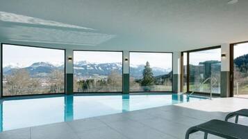 Piscina interior moderna com amplas janelas proporcionando vista para as montanhas.