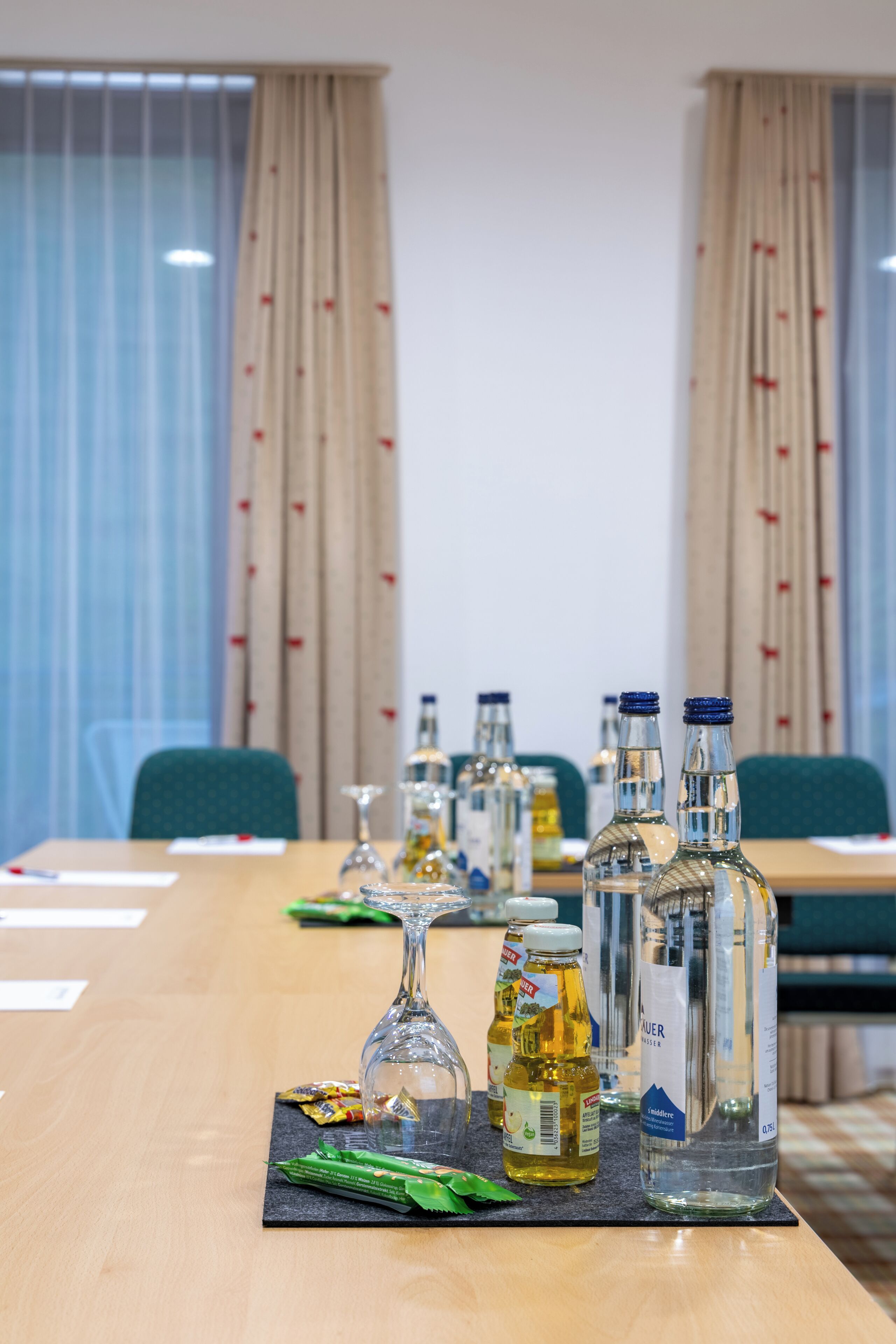 Sala de conferência com uma longa mesa posta para uma reunião, com copos, garrafas e lanches.