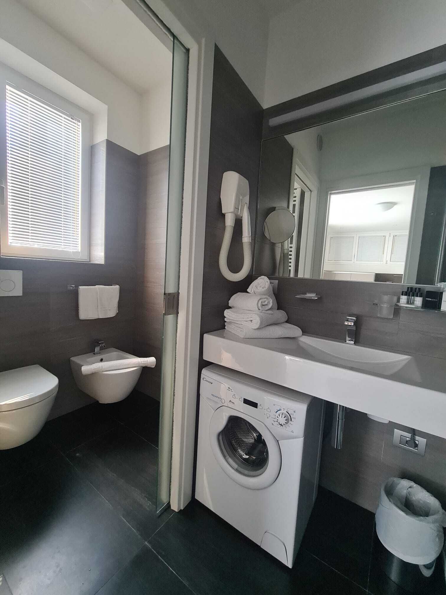 Casa de banho moderna com sanita, bidé, máquina de lavar roupa e um espelho grande.