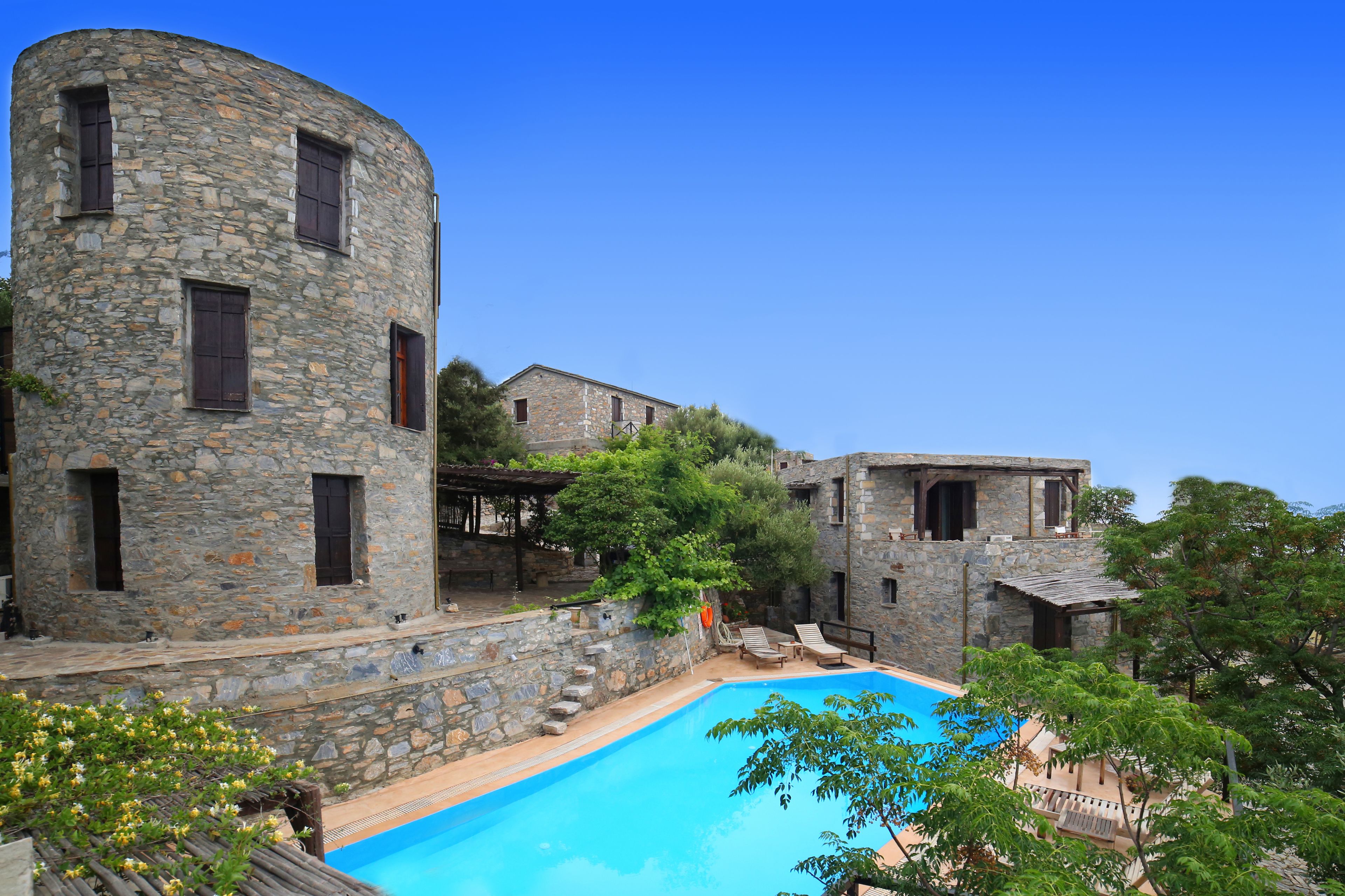 Um edifício de pedra com piscina, cercado por árvores e vegetação.