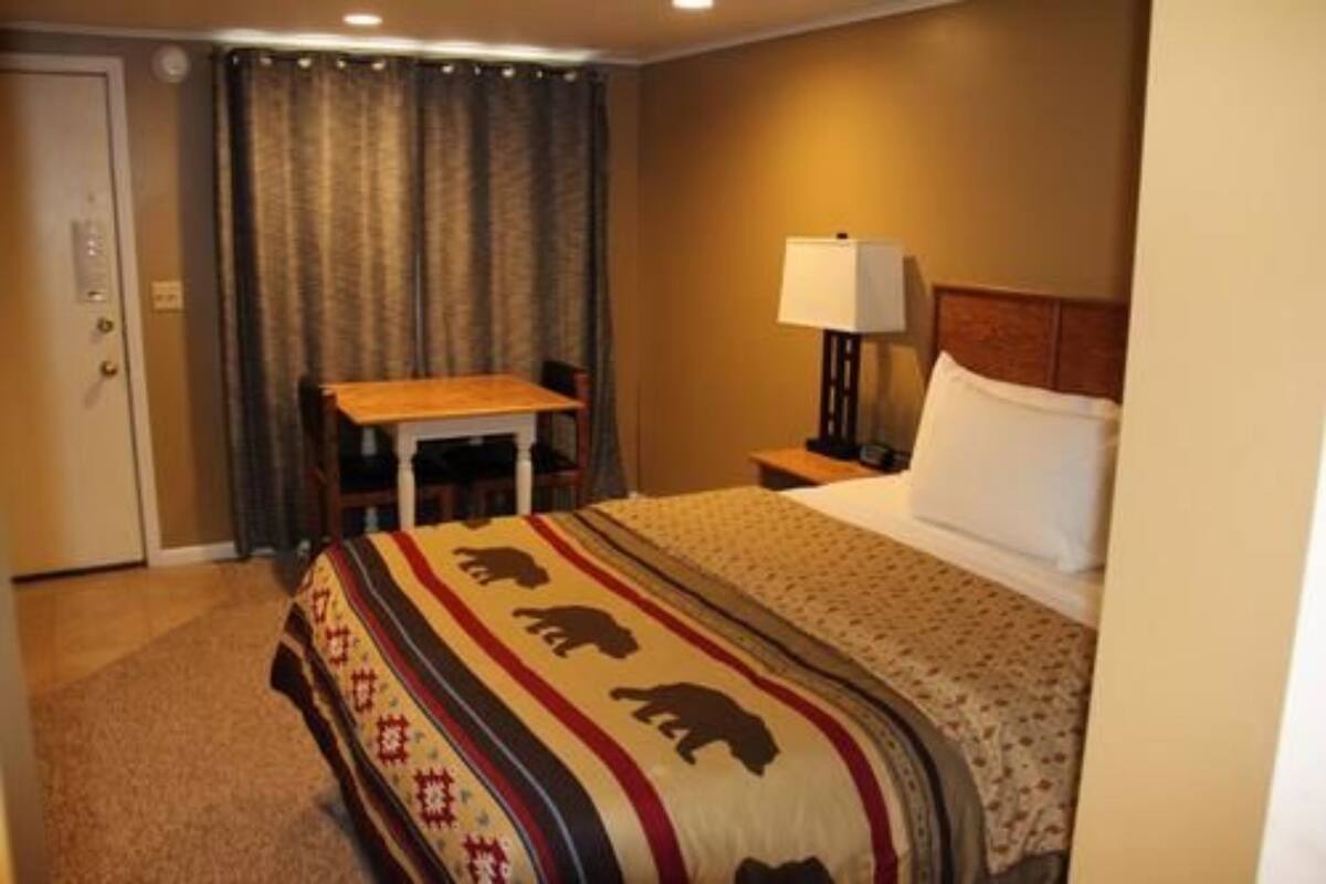 Quarto de hotel com cama, escrivaninha, luminária e porta.