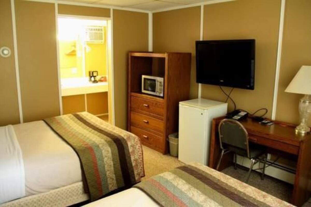 Quarto de hotel com duas camas, uma escrivaninha, uma televisão e um pequeno frigorífico.
