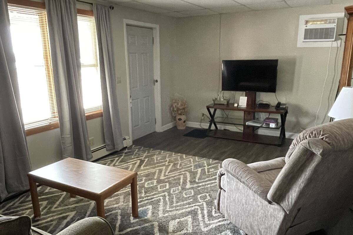 Uma sala de estar com sofá, poltrona e televisão sobre um suporte.