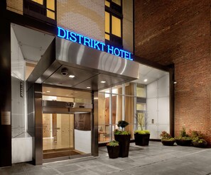 Exterior do Hotel Distrikt, com fachada moderna, grande entrada de vidro e plantas em vasos na frente.