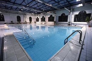 Piscina interior com água azul cristalina, paredes revestidas de azulejos e teto alto com vigas aparentes.