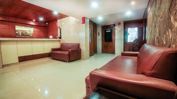 Um hall de entrada com balcão de recepção, um sofá de couro vermelho e área de elevadores.