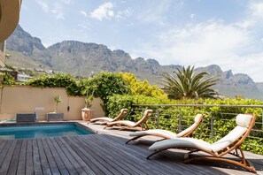 Área da piscina com espreguiçadeiras, piscina e vista para montanhas.
