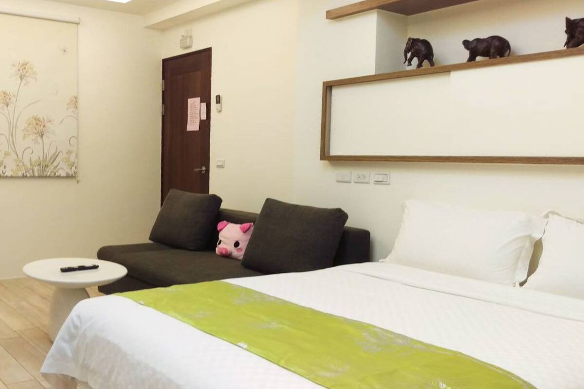 Quarto de hotel com uma cama, um sofá, uma mesinha e uma prateleira na parede com pequenas estatuetas de animais.