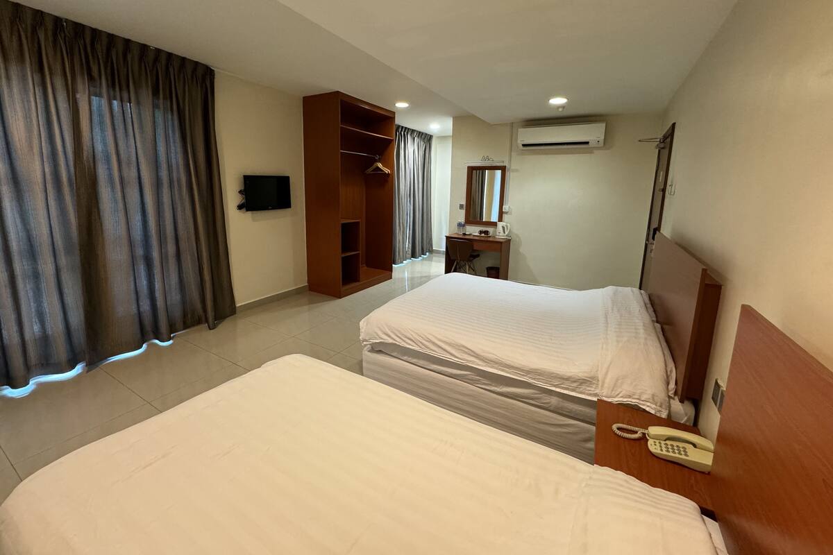 Quarto de hotel com duas camas, uma escrivaninha com cadeira, guarda-roupa, espelho, telefone e ar condicionado.
