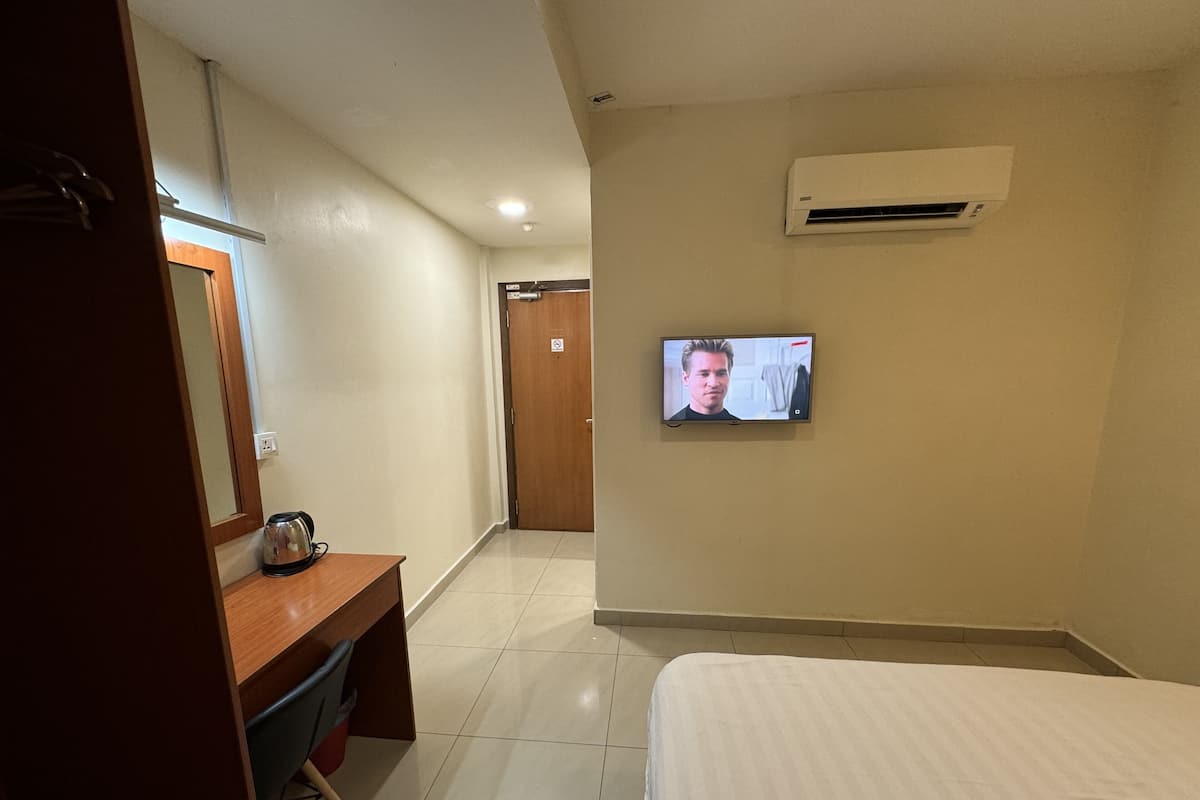Quarto de hotel com cama, escrivaninha com cadeira, televisão na parede e ar condicionado.