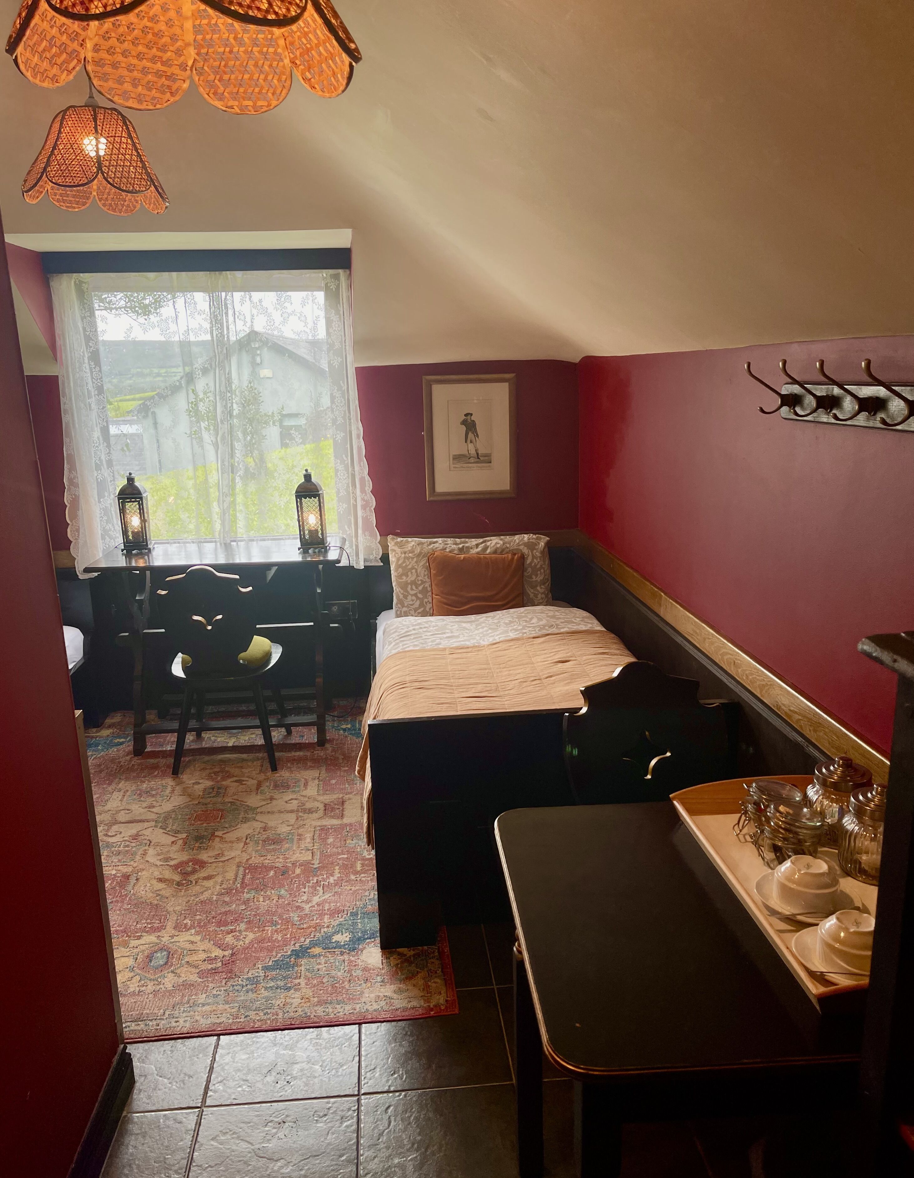 Quarto com cama, escrivaninha e janela com vista para área verde.