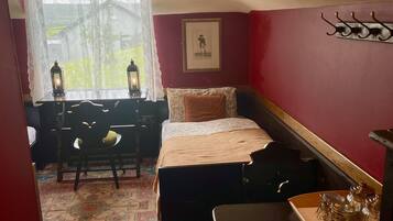 Quarto com cama, escrivaninha e janela com vista para área verde.