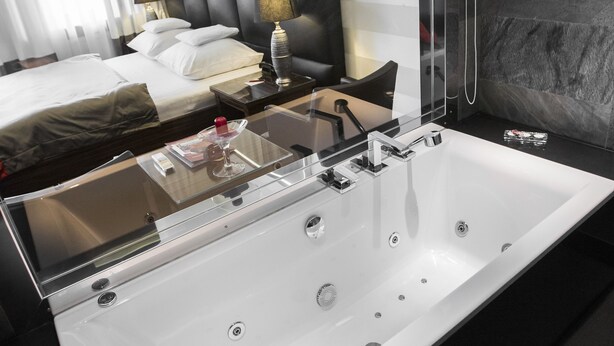 Um banheiro de hotel moderno com uma banheira grande e branca, um espaço para maquiagem com divisória de vidro e um espelho grande.