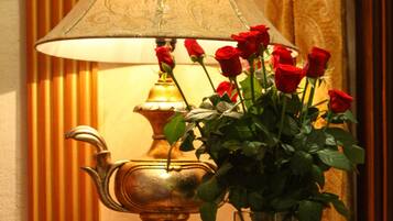 Um abajur com cúpula decorativa e um vaso com rosas vermelhas sobre uma mesa de madeira.
