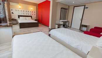 Quarto de hotel com duas camas, uma parede de destaque vermelha, uma escrivaninha pequena e um guarda-roupa.