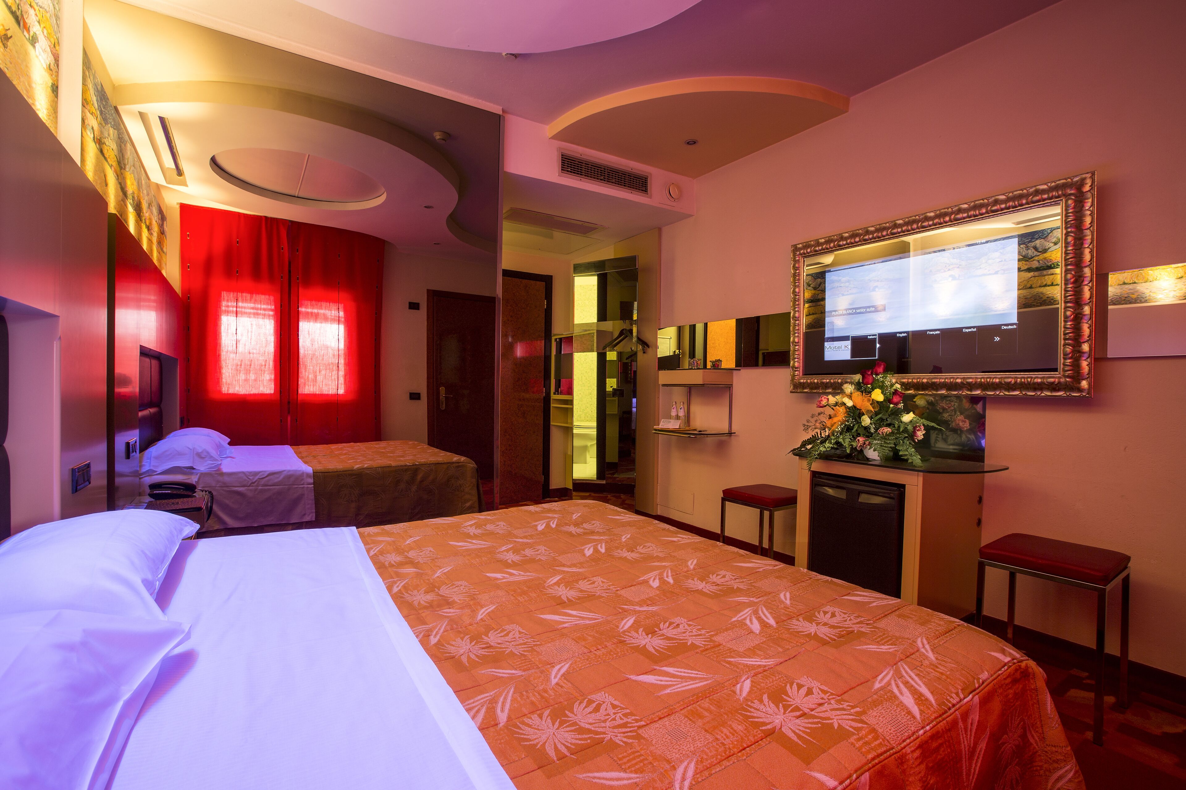 Quarto de hotel com duas camas, televisão, escrivaninha com computador e espelho.