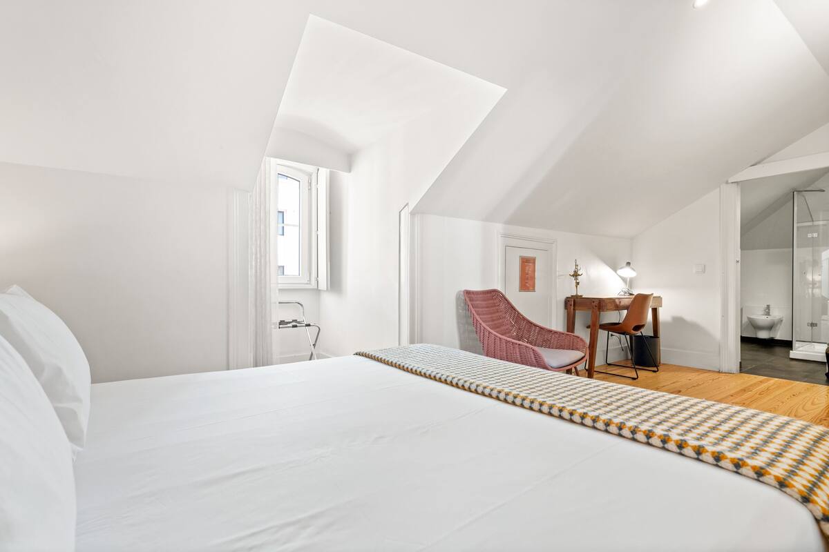 Quarto moderno com uma cama grande, uma escrivaninha com cadeira, uma cadeira vermelha e área de chuveiro.