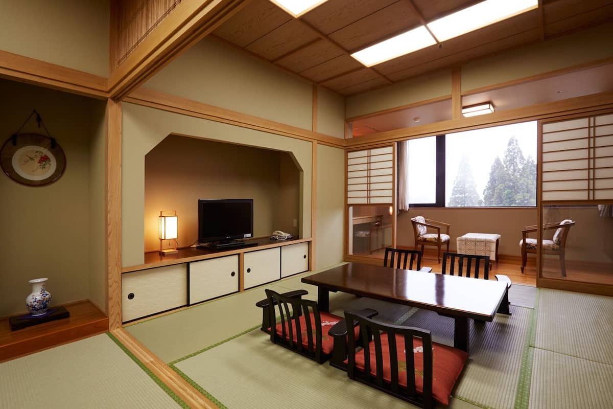 Quarto japonês tradicional com tatames, uma mesa baixa com cadeiras, televisão e porta deslizante.