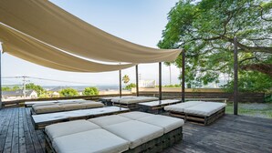 Um deck com várias espreguiçadeiras e colchões, um toldo acima e vista para a paisagem.