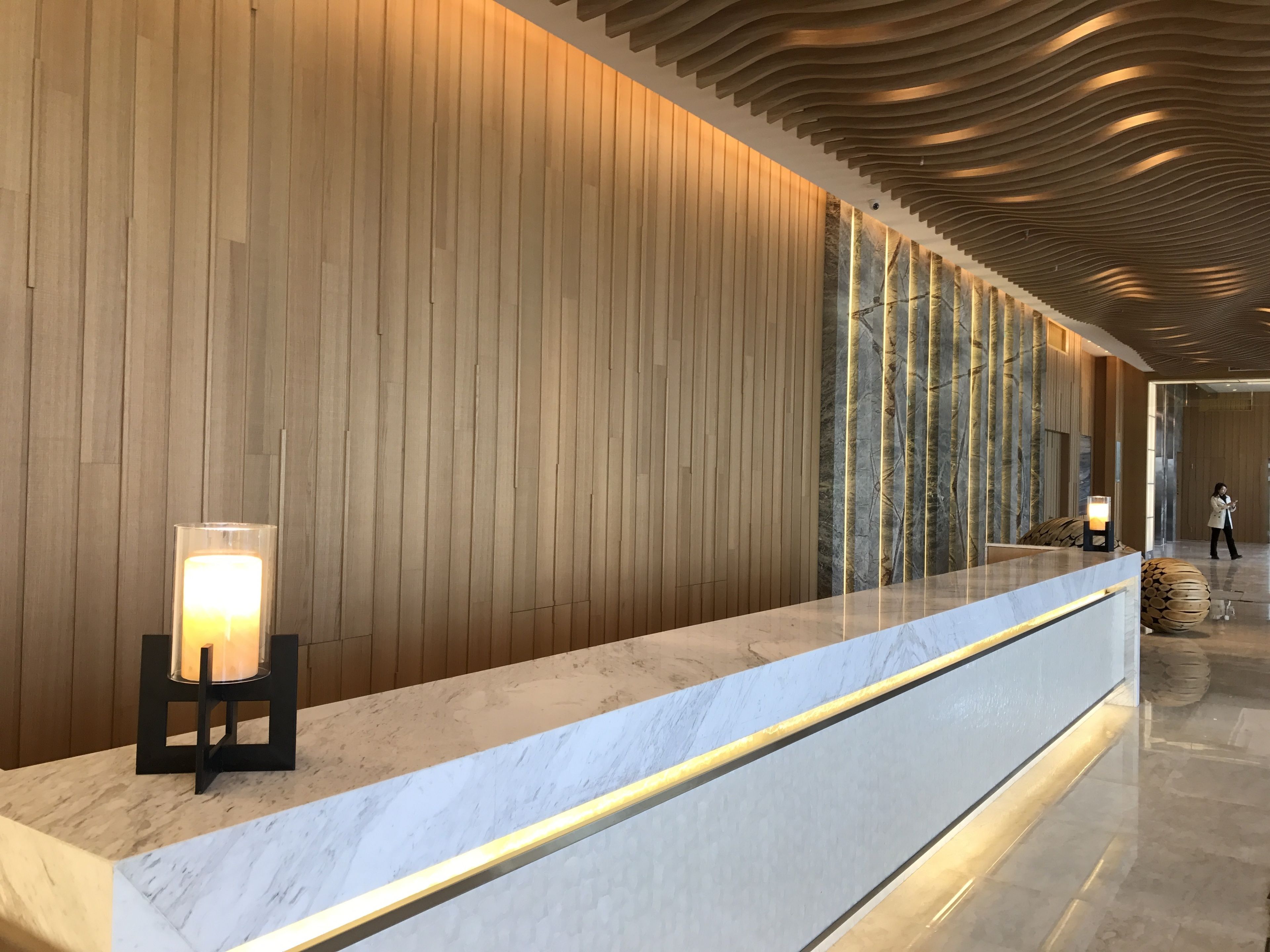 Uma área de recepção moderna com balcão de mármore, painéis de madeira e um design de teto único.