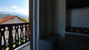 Uma cozinha com fogão e armários, uma janela com vista para montanhas e uma varanda com design único na grade.