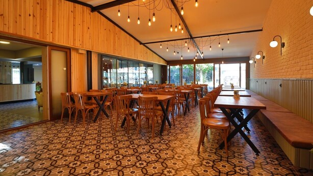 Uma sala de jantar ampla com mesas e cadeiras de madeira, azulejos com padrão e luminárias pendentes.