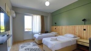 Quarto de hotel com duas camas, uma televisão e cabeceira de madeira.