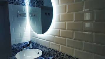 Casa de banho com lavatório branco, azulejos com padrão azul e espelho redondo com iluminação embutida.