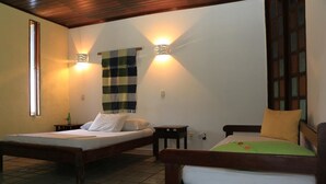 Quarto com duas camas de madeira, uma mesinha e luminária fixada na parede.