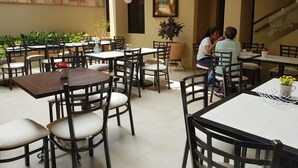 Área de refeições ao ar livre com várias mesas e cadeiras, plantas em vasos e uma escadaria para um andar superior.