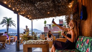 Um bar no terraço com móveis de vime, luzes de corda e vista para as montanhas.