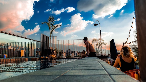 Piscina externa com vista para o horizonte urbano, corrimão e algumas pessoas relaxando.