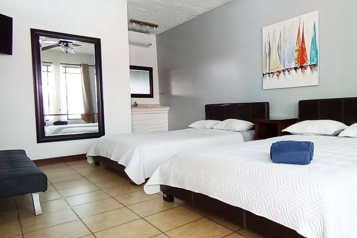 Quarto de hotel com duas camas, um espelho, um quadro e um banco de madeira.