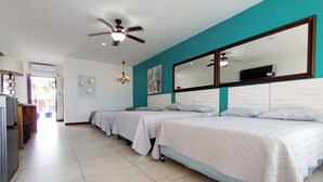 Quarto de hotel com duas camas, ventilador de teto, espelho grande e vista para o exterior.