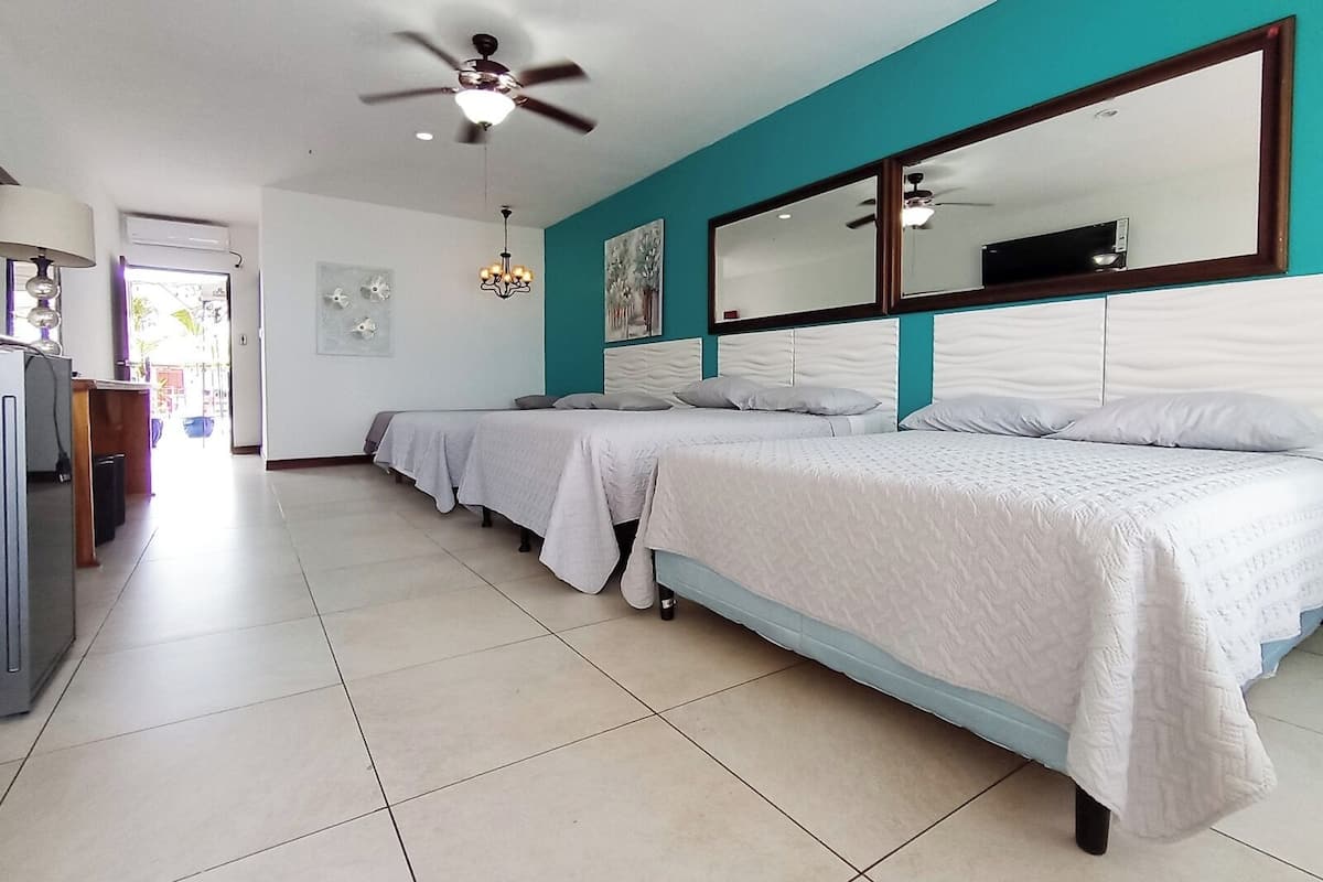 Quarto de hotel com duas camas, ventilador de teto, espelho grande e vista para o exterior.