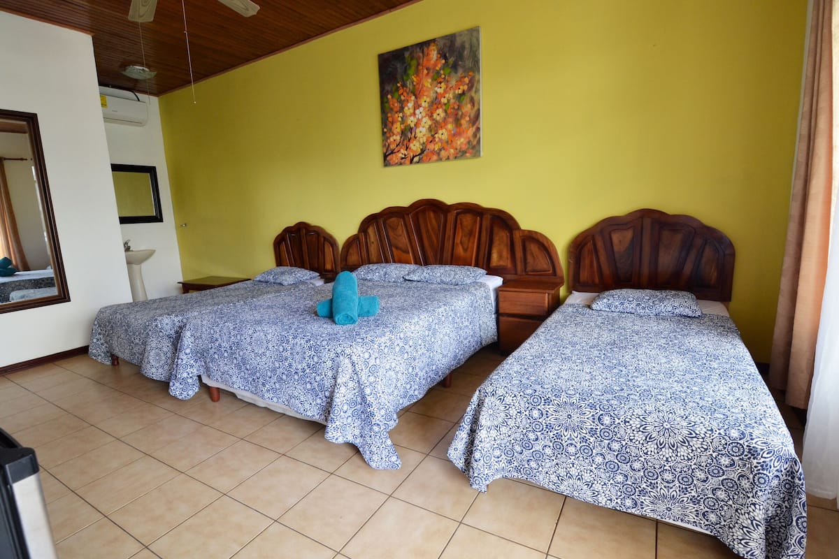 Quarto de hotel com duas camas, cabeceira de madeira, um quadro na parede e uma pia.