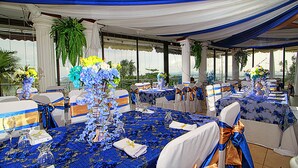 Salão de festas com mesas montadas para um evento formal, com toalhas azuis e douradas e arranjos florais.